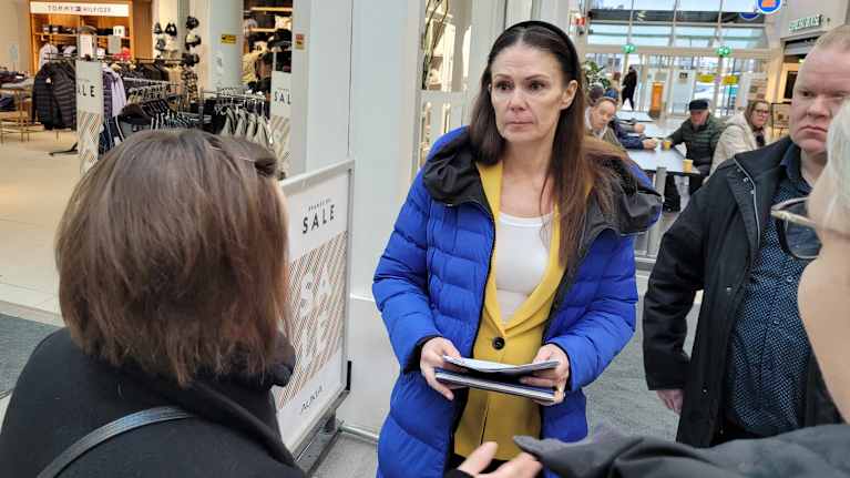 Liikenne- ja viestintäministeri Lulu Ranne (ps.) seisoo ihmisjoukossa ja tapaa kansalaisia kauppakeskuksessa. 