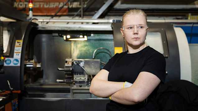 Nuori nainen seisoo kädet puuskassa CNC-koneen äärellä.