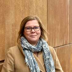 Hanna Laine (sd.), Kangasalan kaupunginvaltuuston puheenjohtaja. Laineella on beige villakangastakki ja sini-valkoinen huivi sekä silmälasit. Hän seisoo ruskeaa seinää vasten. Kuvauspäivä 27.3.2024.