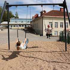 Tytöt keinuvat koulun pihassa.