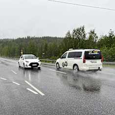 Kaksi valkoista autoa liikkuu kantatiellä 62 sateisena kesäpäivänä.