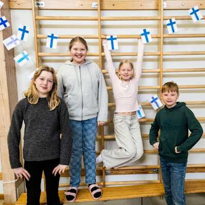 Fyra skolever står framför en vägg med ribbstolar. Finska flaggor hänger på väggen.